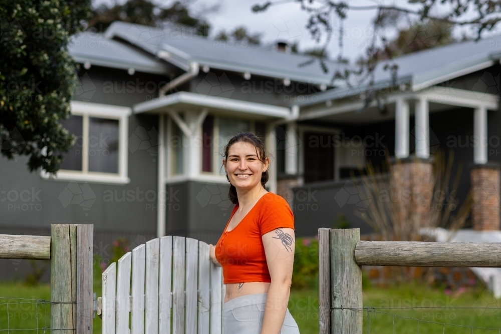 Image of young woman at the front of her home opening the gate ...