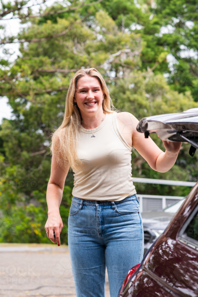 Image of young woman closing the hatch on her car - Austockphoto
