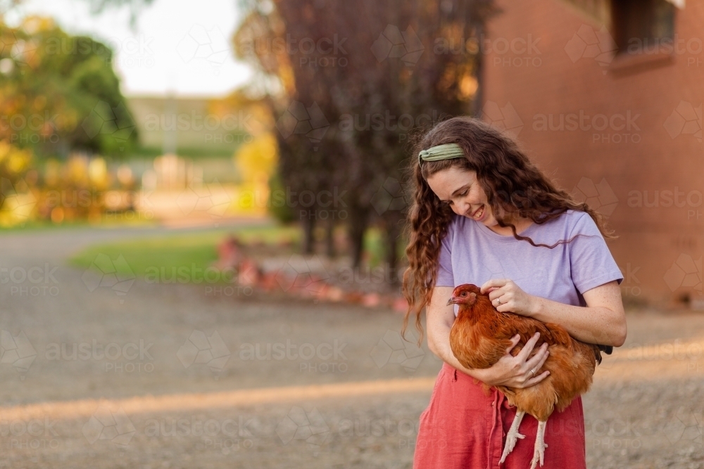 Image of Young woman in country holding chook in arms with copy space ...