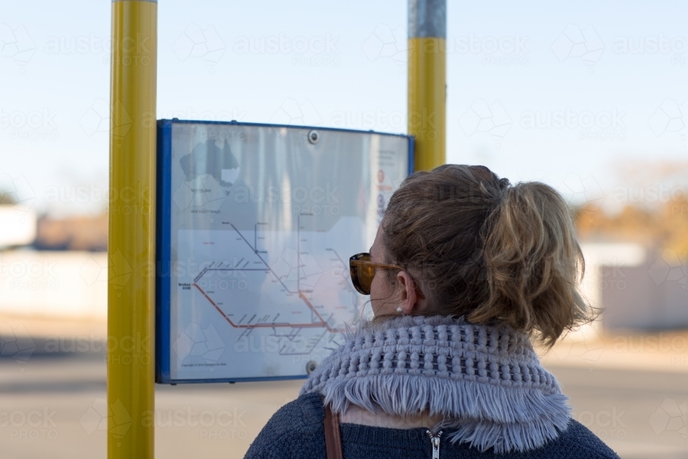 Image of Young woman looking at sign with bus routes - Austockphoto