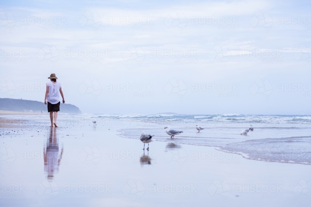 Image of Young woman walking along beachcombing looking for shells at ...